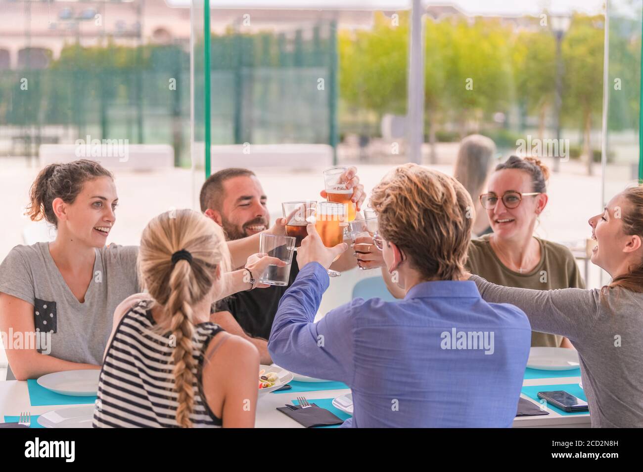a group of smiling young people doing a toast over a table on an out of ...