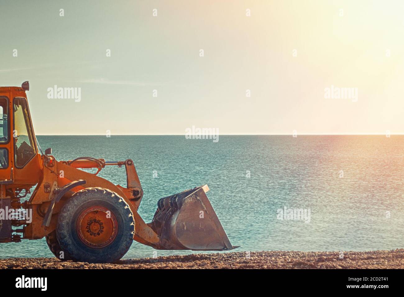Yellow bulldozer rides on the beach. In the background sea and sky ...