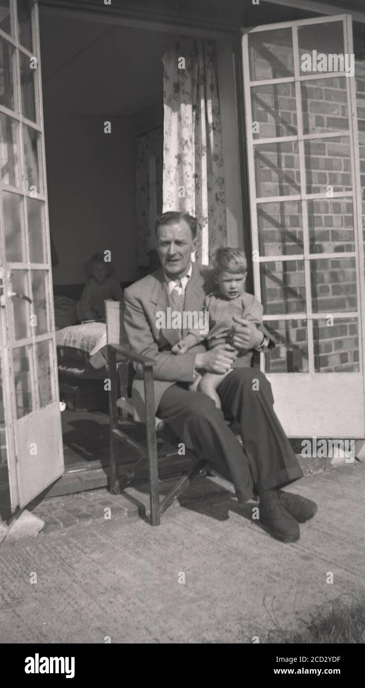 1950s, historical, a father sitting with his young son outside the ...