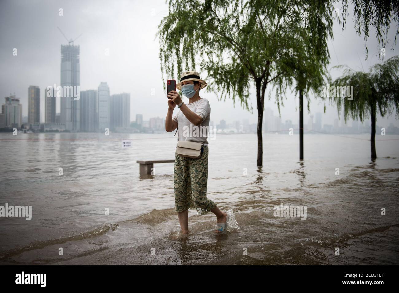 Citizens walk along the waterlogged riverside road in Wuhan city ...