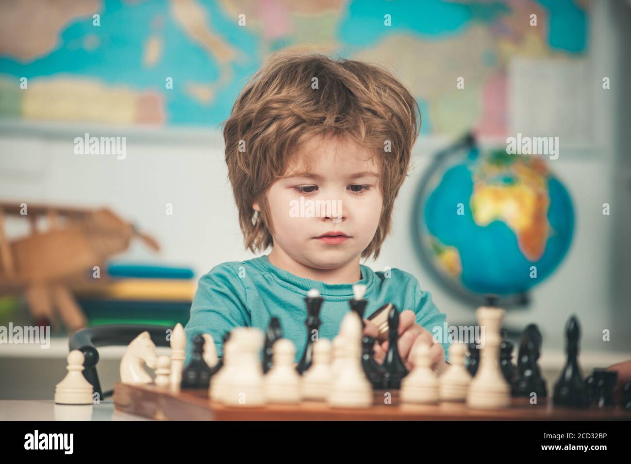 Concentrated little boy sitting at the table and playing chess. Boy kid ...