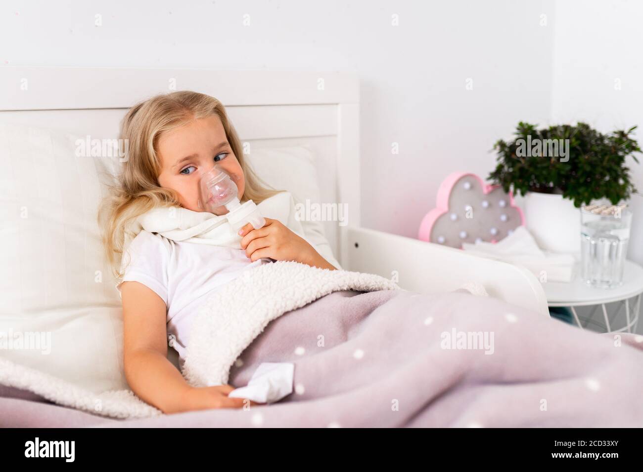 Little girl makes inhalation with a nebulizer in the house lying in bed ...