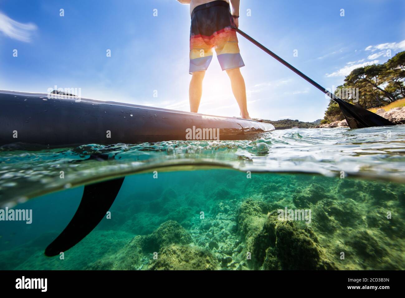 Detail of young man on paddleboard, half under and half above water ...