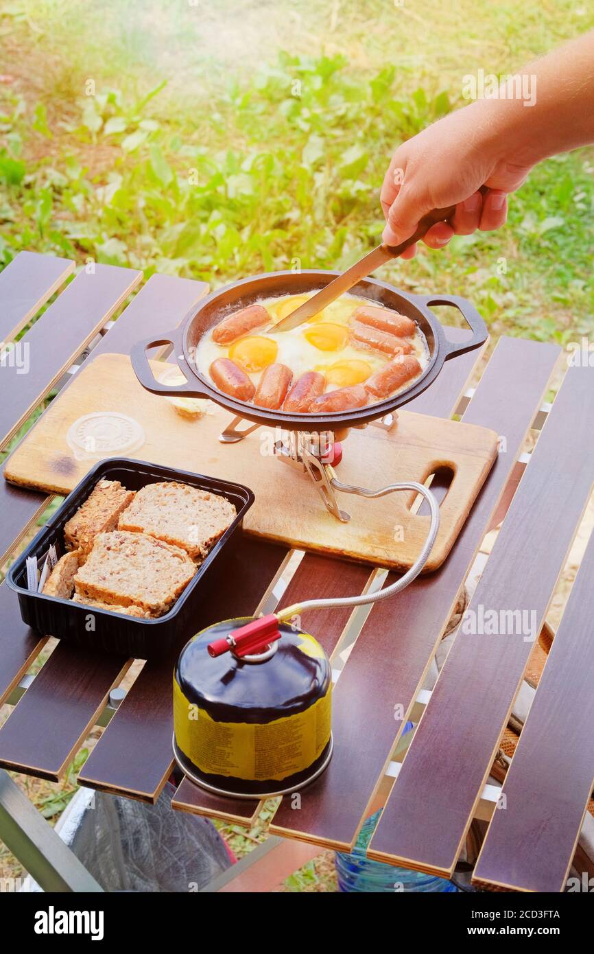 Camping food making. Fried eggs and sausages on pan on tourist gas ...