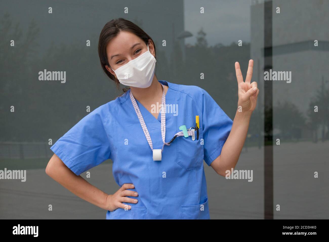 A beautiful young nurse happily makes the victory sign with her hand ...