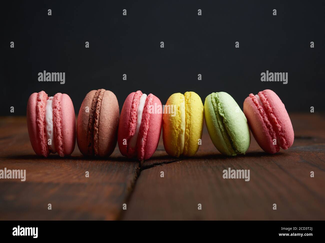 baked multi-colored macarons cookies lie in a row on a brown wooden ...