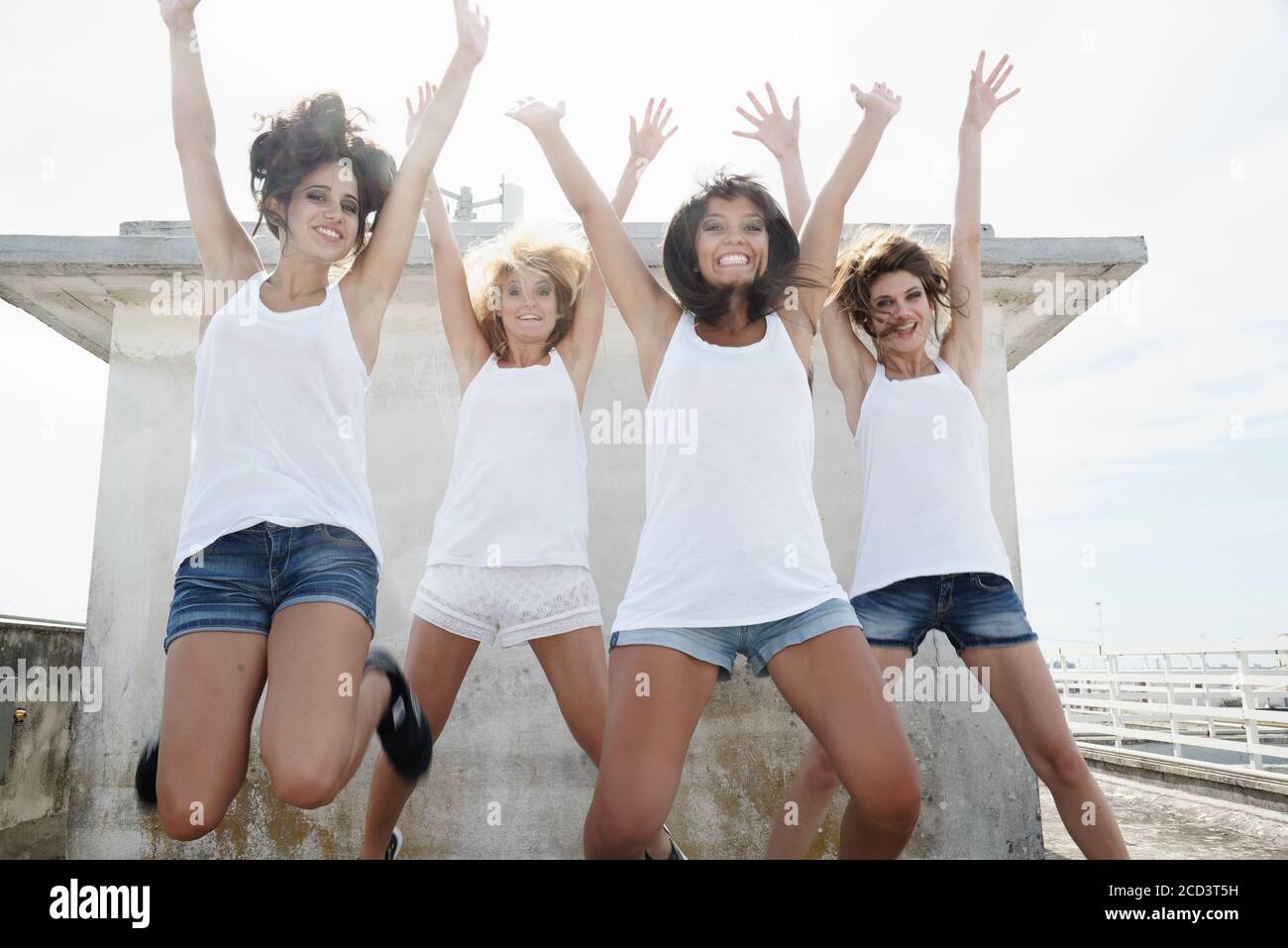 Portrait of four young women having fun, leaping into air with arms ...