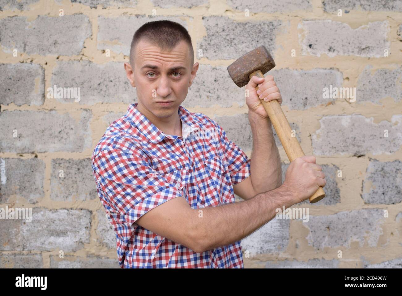 Angry man with sledgehammer on the brick wall background. Working ...