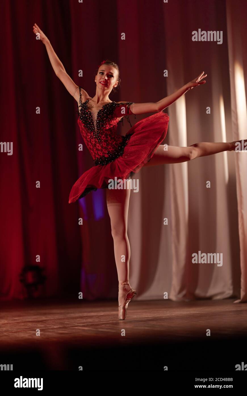 Young girl ballerina in a red tutu performs with a performance on stage ...