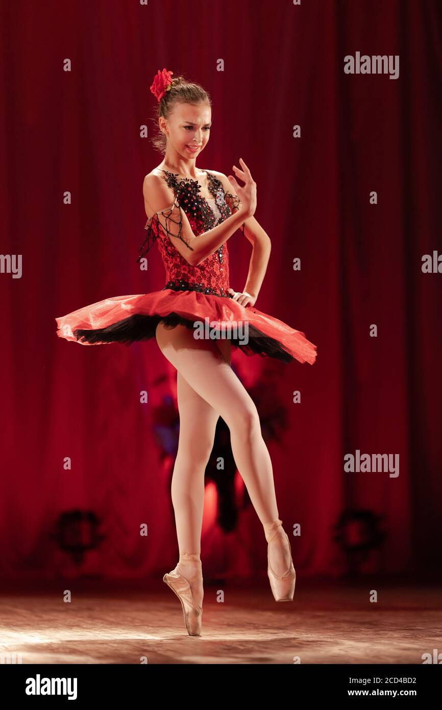 Young girl ballerina in a red tutu performs with a performance on stage ...