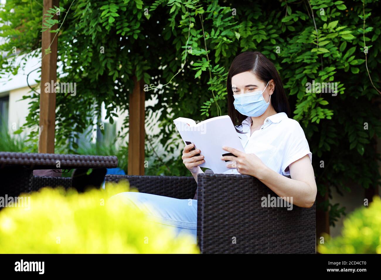 A woman in a mask is reading a book while sitting in a cafe. A lonely ...