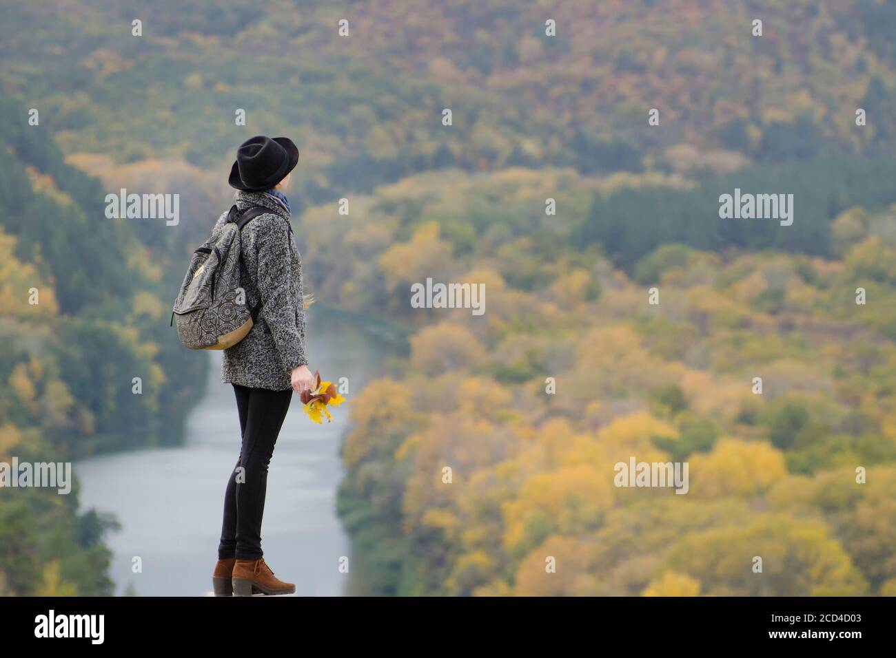 Girl with a backpack and a hat standing on a hill. Hands raised up ...