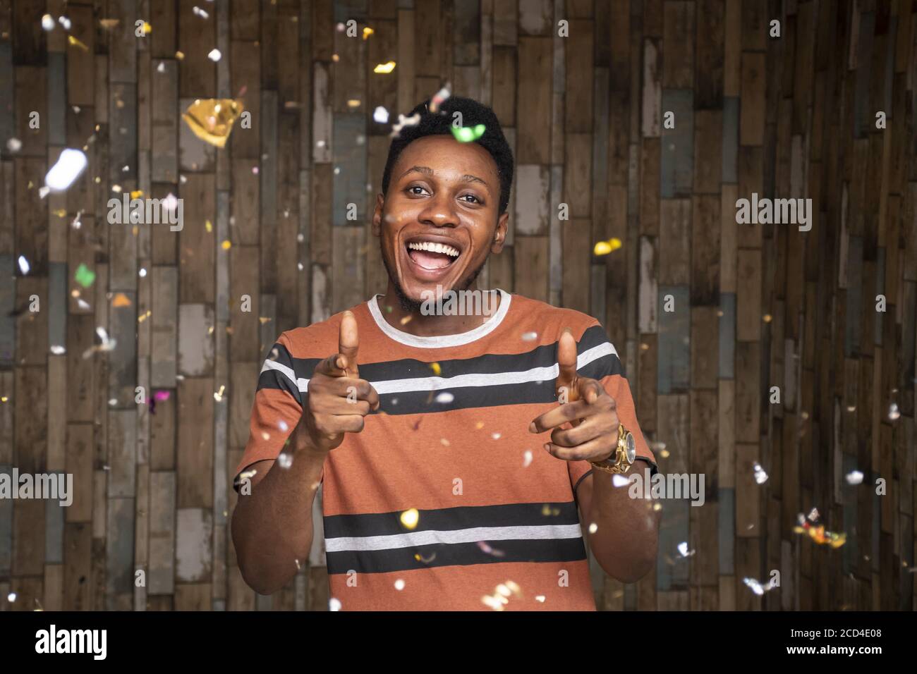 Happy African male celebrating with confetti in front of a wooden wall ...