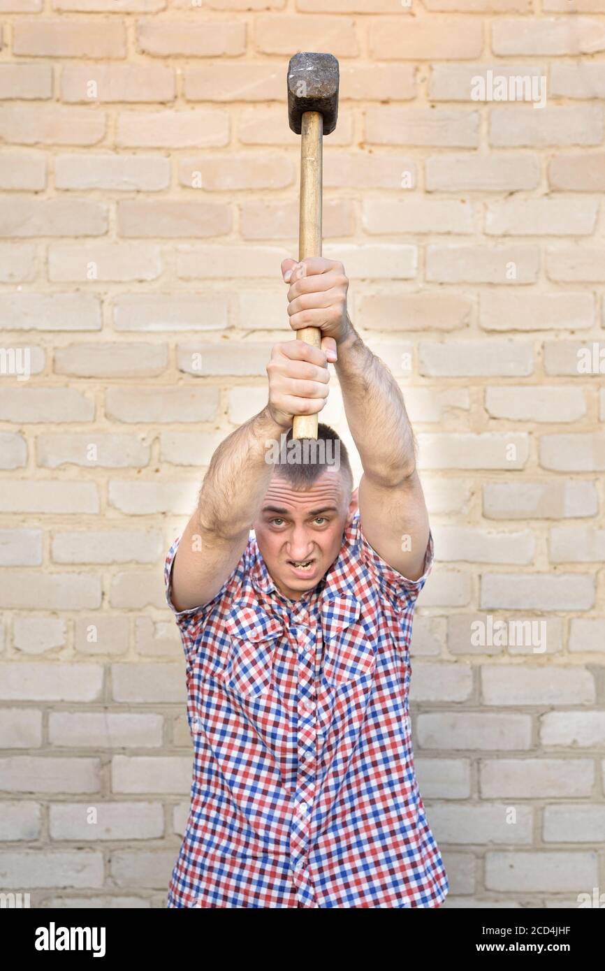 Angry man with sledgehammer on the brick wall background. Working ...
