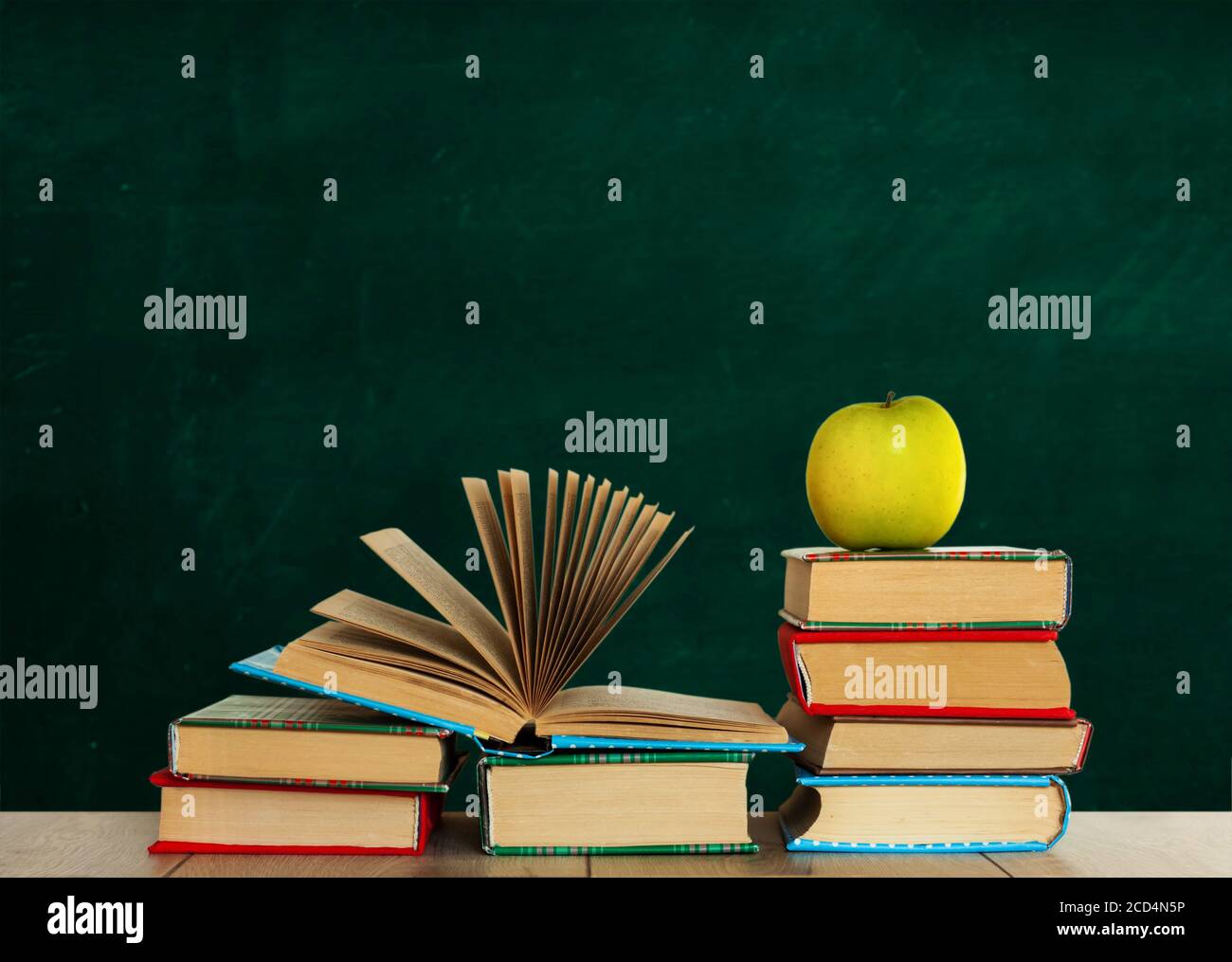 Open textbook, pile of books in colorful covers and green apple on ...