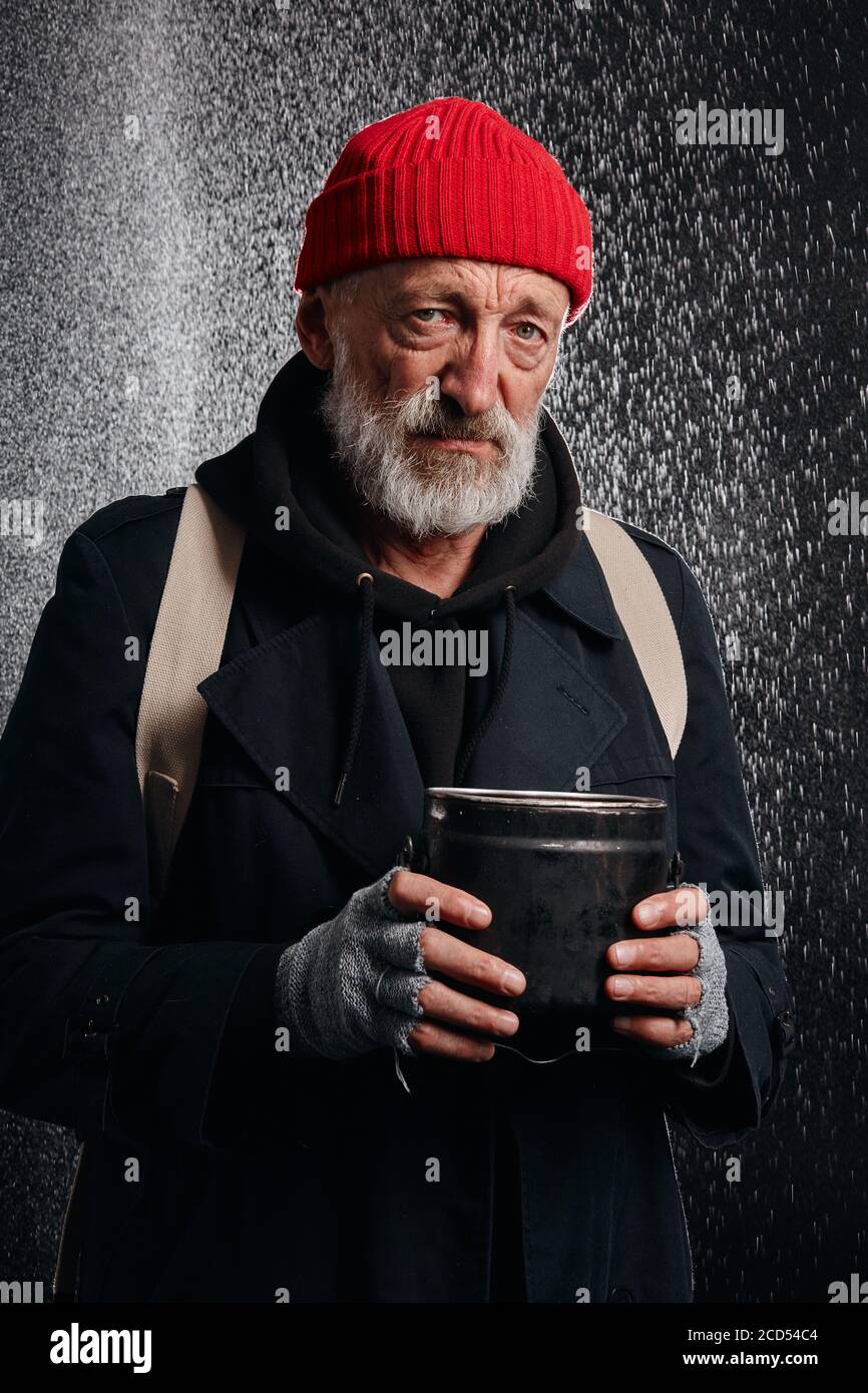 Portrait of homeless man in black street clothes holding iron can for ...