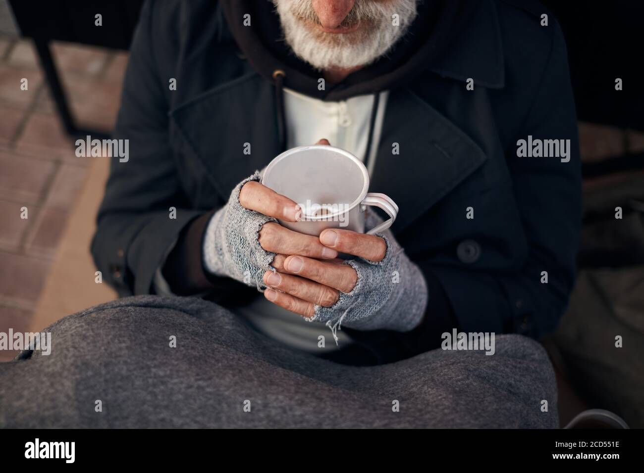 Homeless man's hands holding half empty mug with some coins at bottom ...