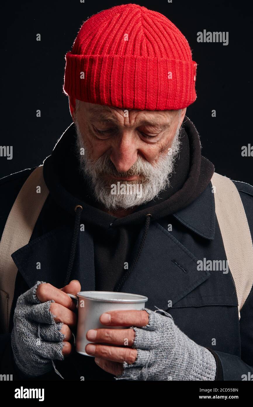 Tired and sick homeless male in coat and red hat look with sadness at ...
