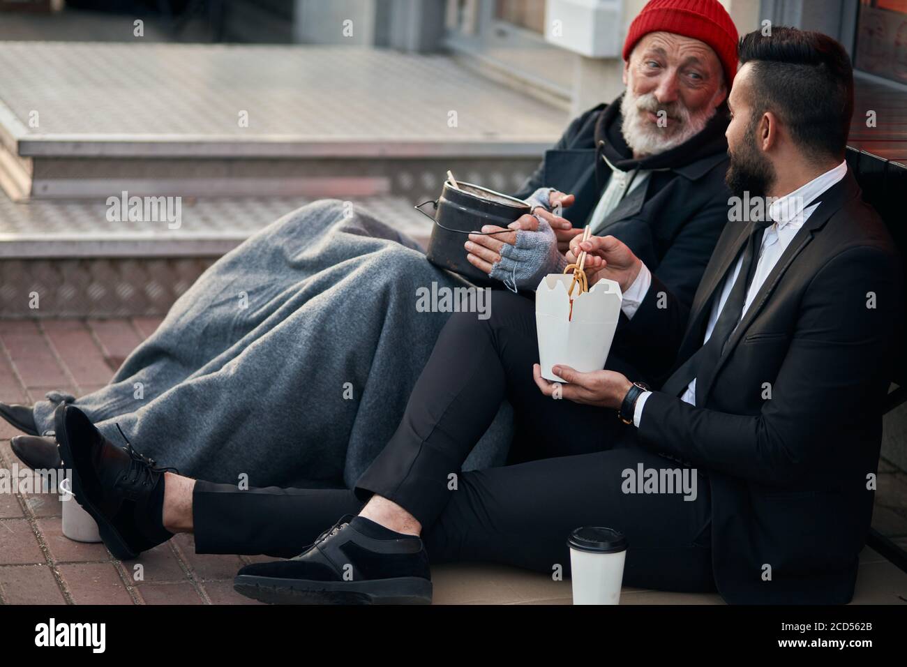 Handsome businessman in suit sitting on floor with homeless man ...