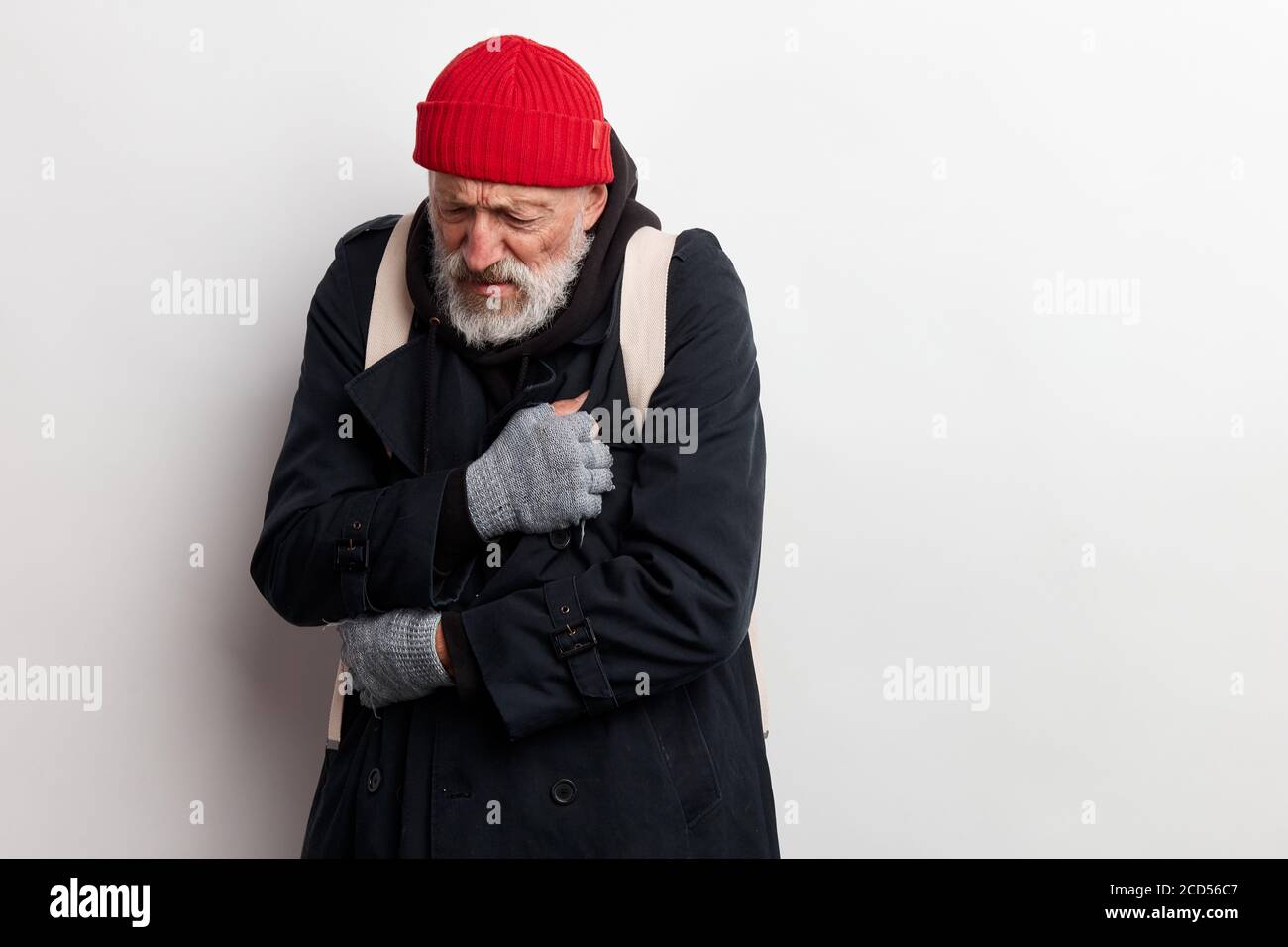 Mature bum, homeless old man in coat and red hat try to warm up ...