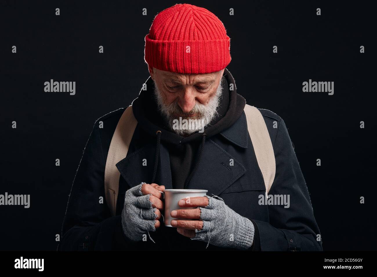 Tired and sick homeless male in coat and red hat look with sadness at ...