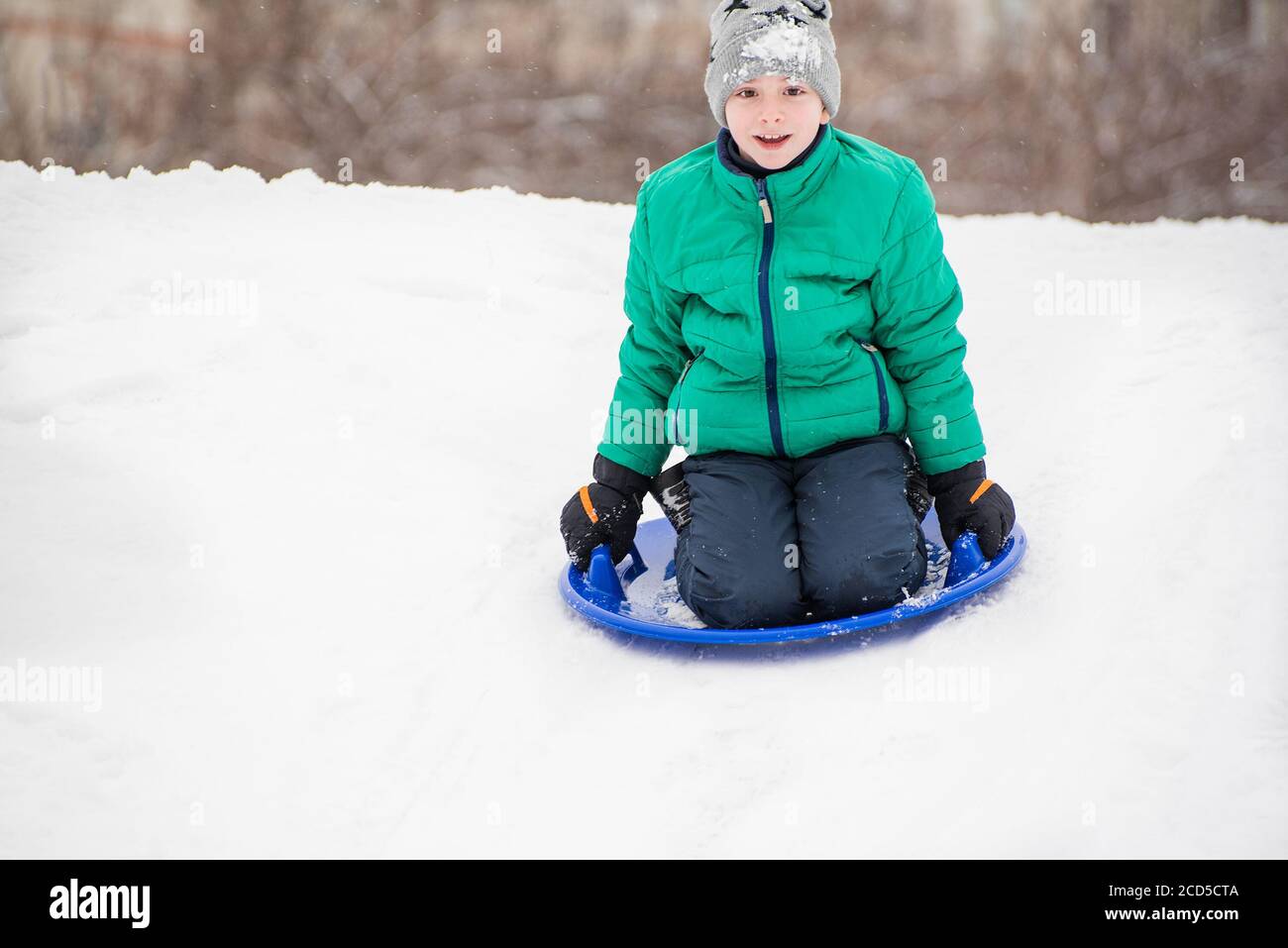 Happy boy slides down the hill on snow saucer. Seasonal concept. Winter ...