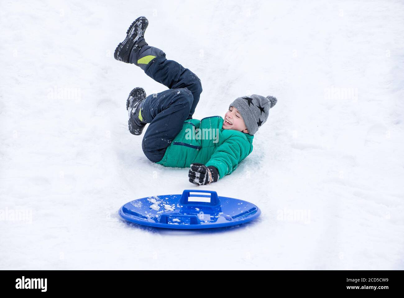 Boy falls rolling down a hill on snow saucer. Winter games Stock Photo ...