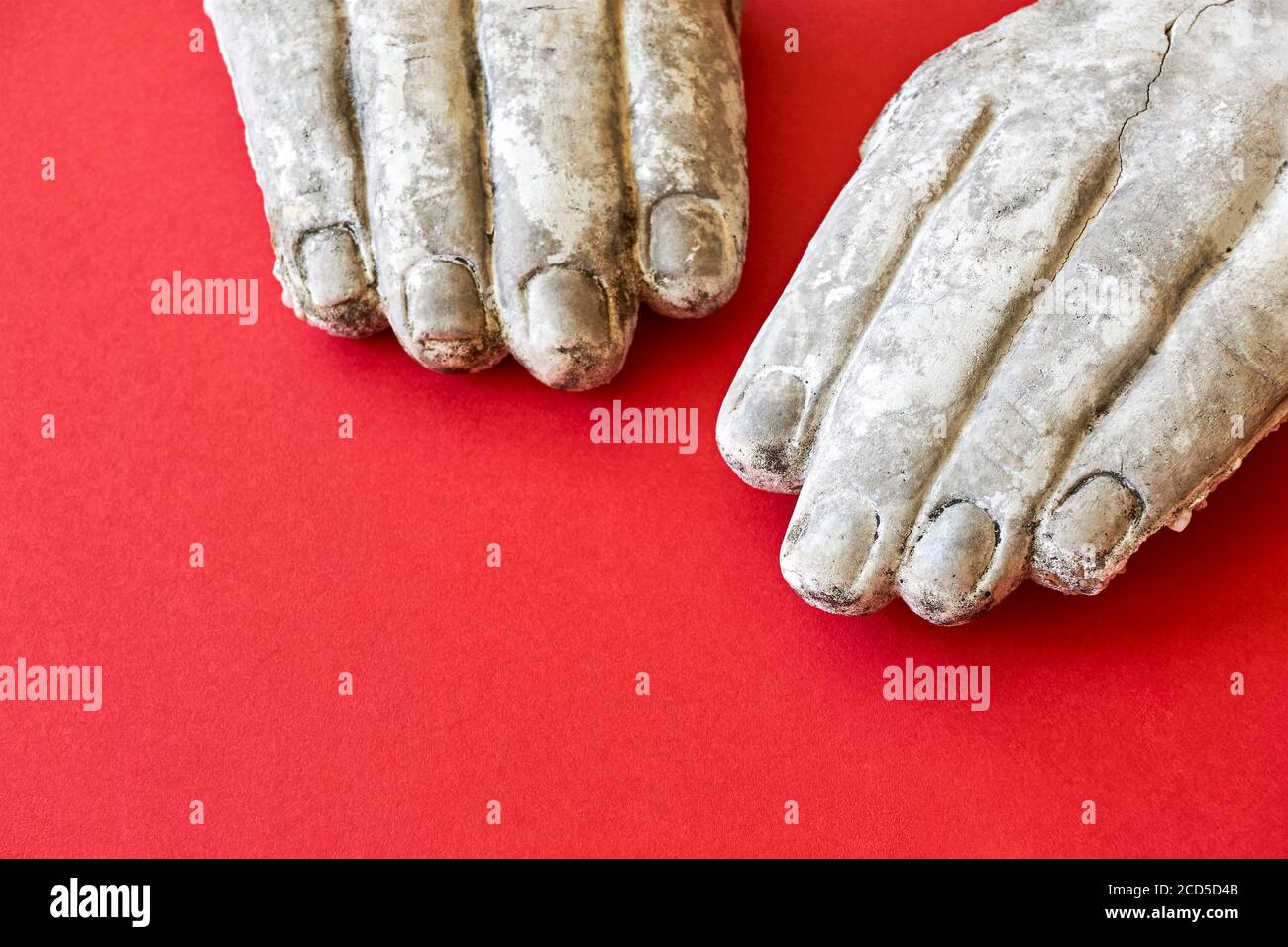 Two white weathered broken hands of a stone statue on a red background ...