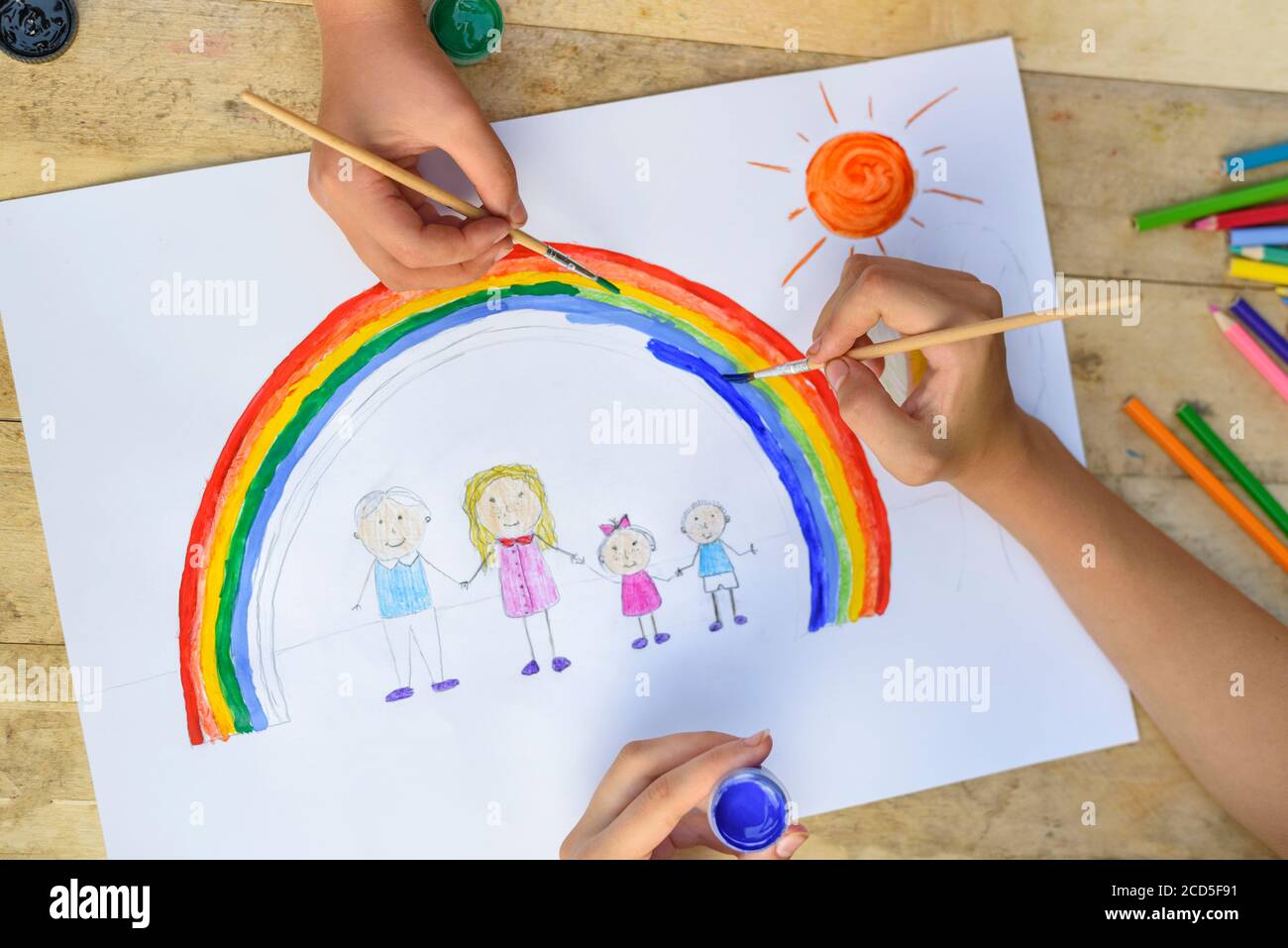 Two children's hands draw a drawing with a brush and paints. Top view ...