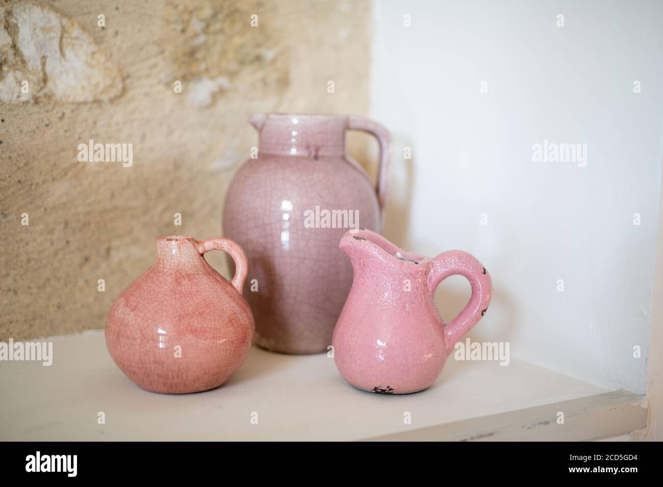 Three pink ceramic pitchers with a stone wall background Stock Photo ...