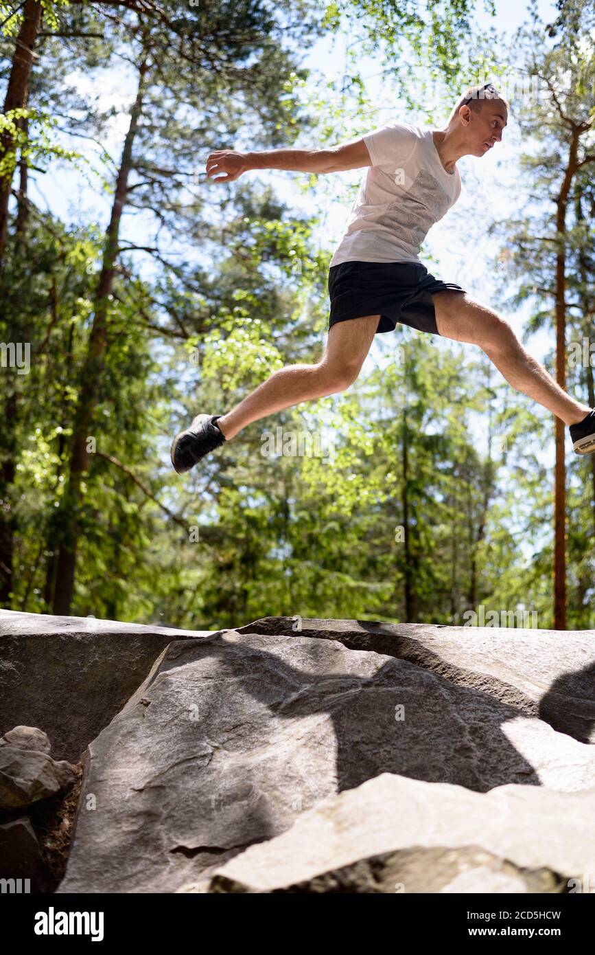 Young man jumps on a rock in a coniferous forest. Active extreme ...
