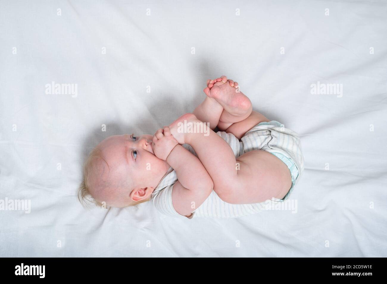 Baby nibbles his leg on white bed. Cute 3 months baby Stock Photo - Alamy