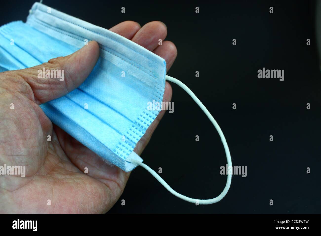 Person's hand holding a face mask isolated on black background ...