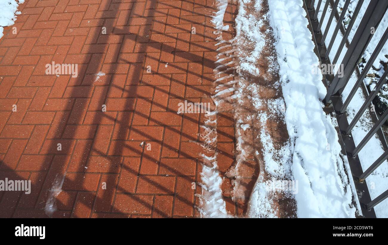 Red paving slabs with melting snow and footprints on it and shadow from ...