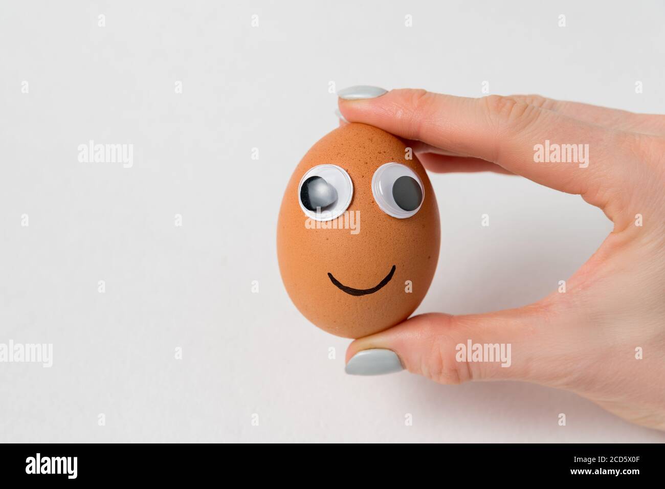 Female hand holding egg-smiley with googly eyes on white background ...