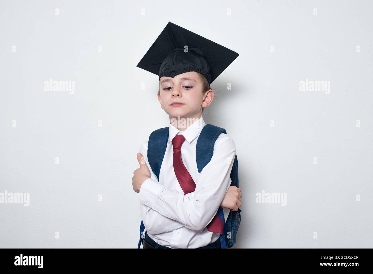Serious boy in school uniform and graduate hat on white background ...