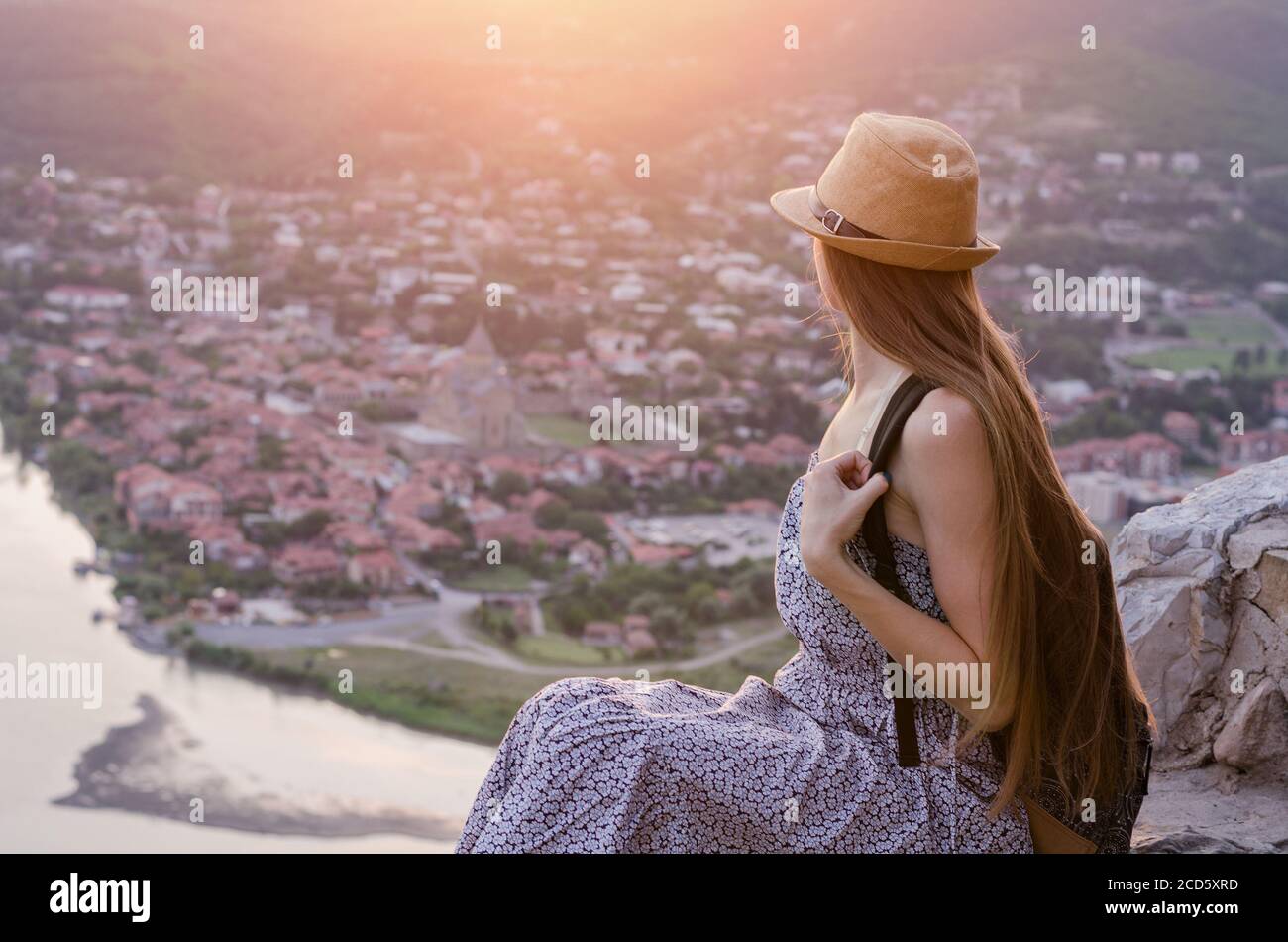 Young attractive girl sitting on hill looking at panorama of city in ...