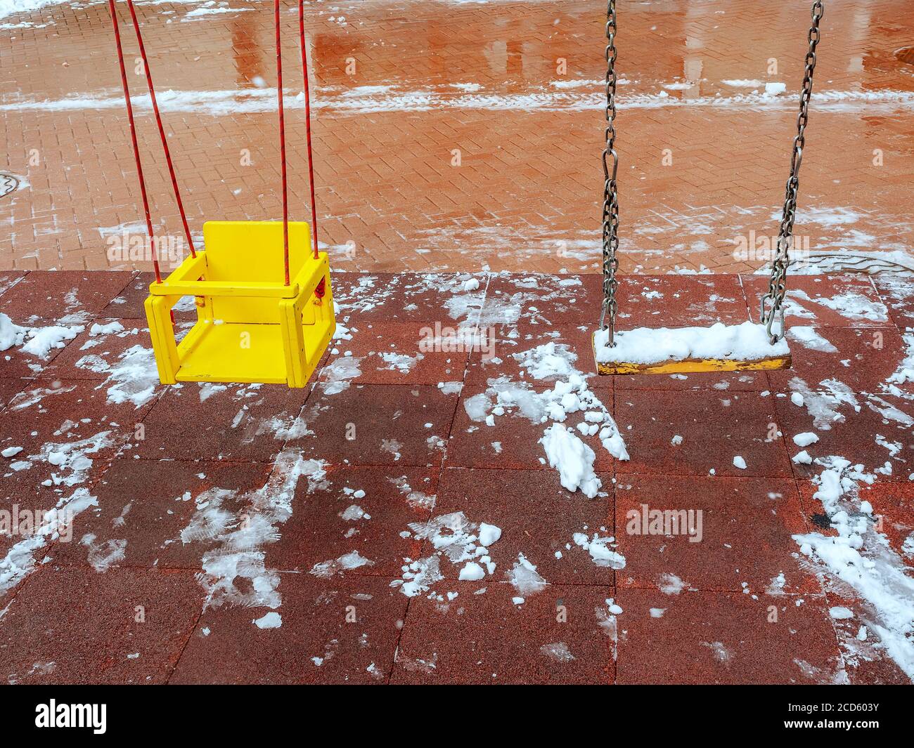 Yellow swing hanging over red paving slabs with melting snow Stock ...