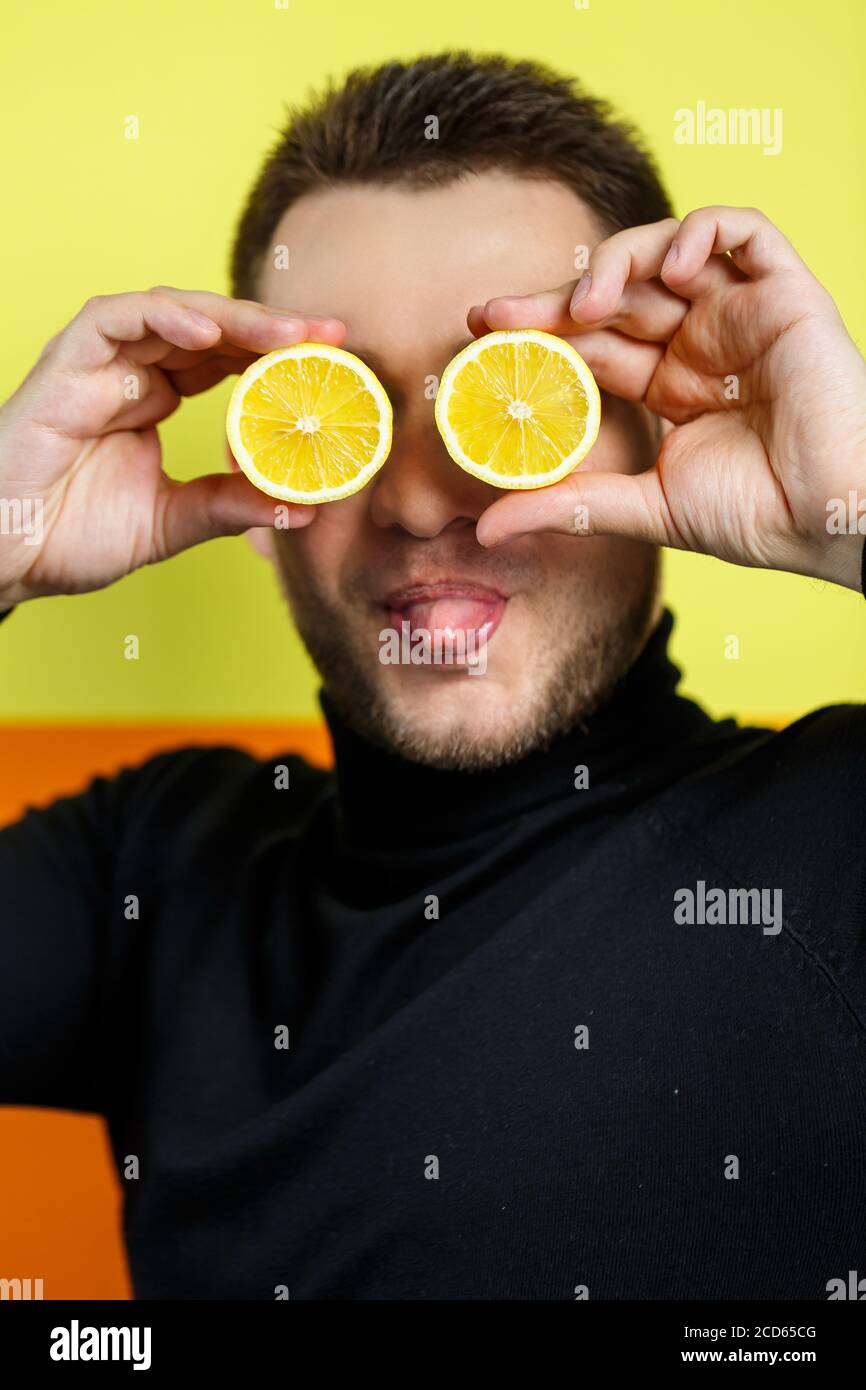 Portrait of a man on a yellow background in black raglan with cut lemon ...