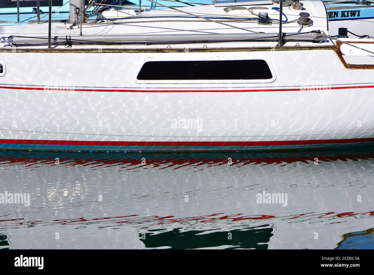 White sailboat hull with red strip reflecting in calm water of marina ...