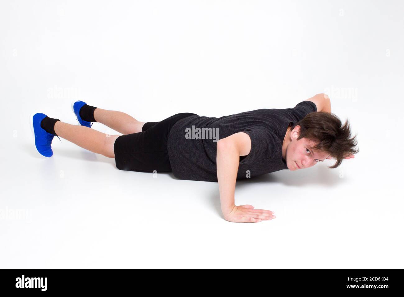 A young boy in a black sports t-shirt and shorts, blue sneakers, trains ...