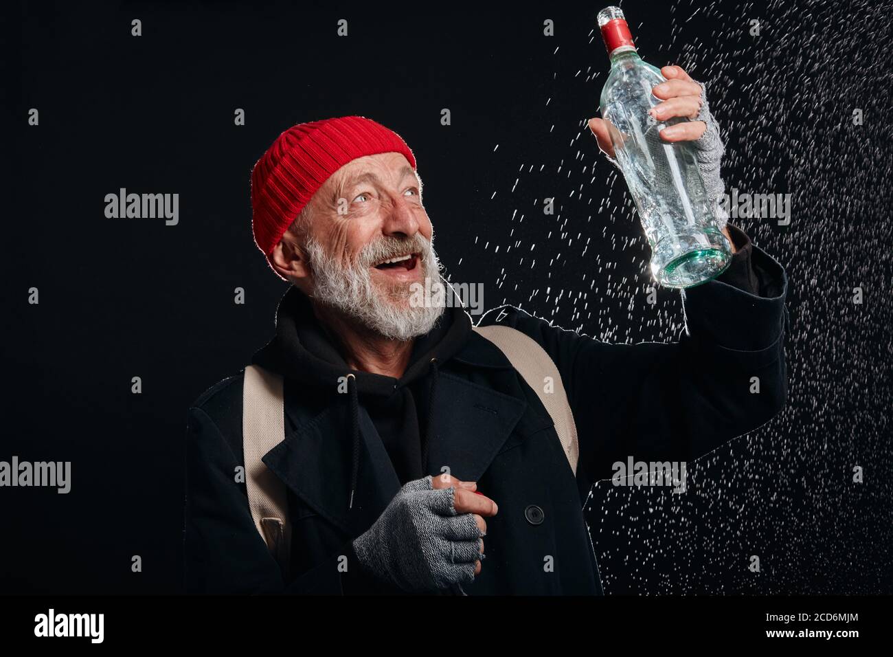 Smiling bum happily look at bottle of alcohol. Homeless male dressed in ...