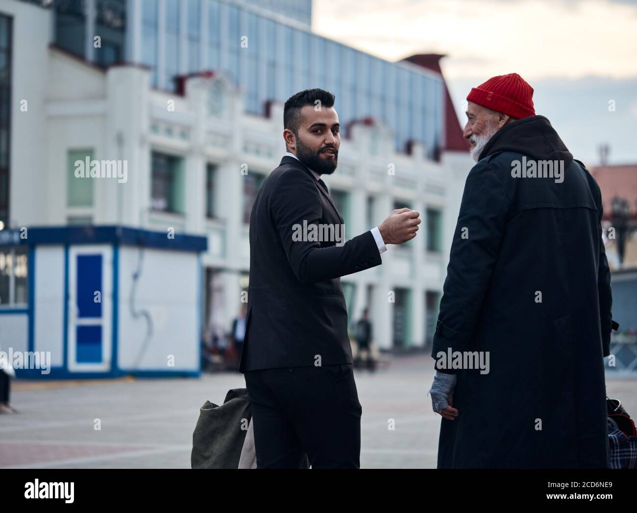 Rich man decided to help poor man. Young bearded man in black suit with ...