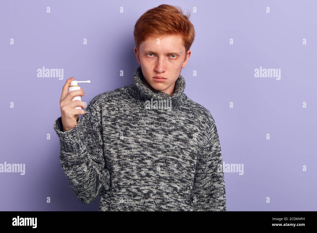 A sick poor man holding a nasal spray in his hand on blue background ...