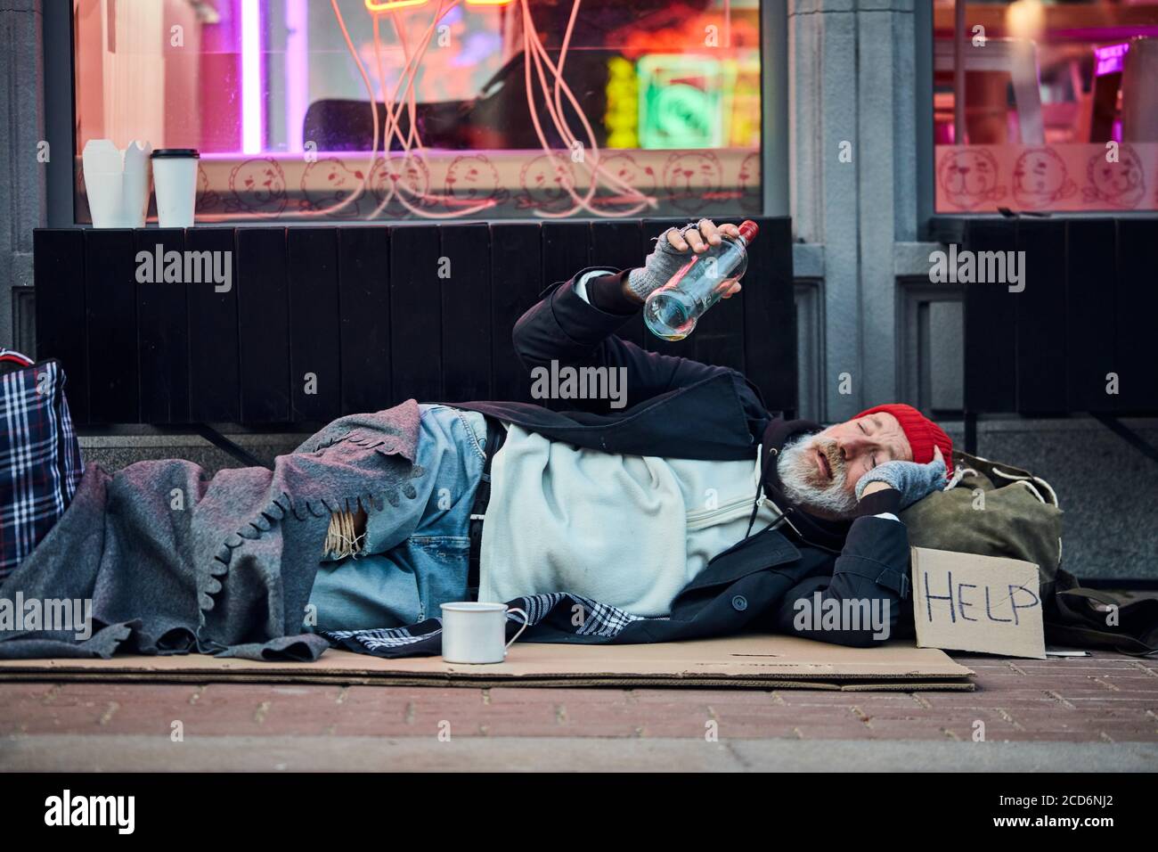 needy beggar male lying on cardboard box with sign HELP and bottle of ...