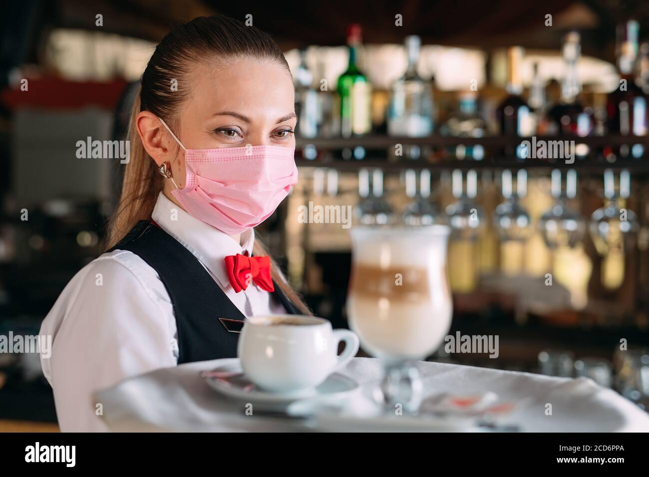 A female Waiter of European appearance in a medical mask serves Latte ...