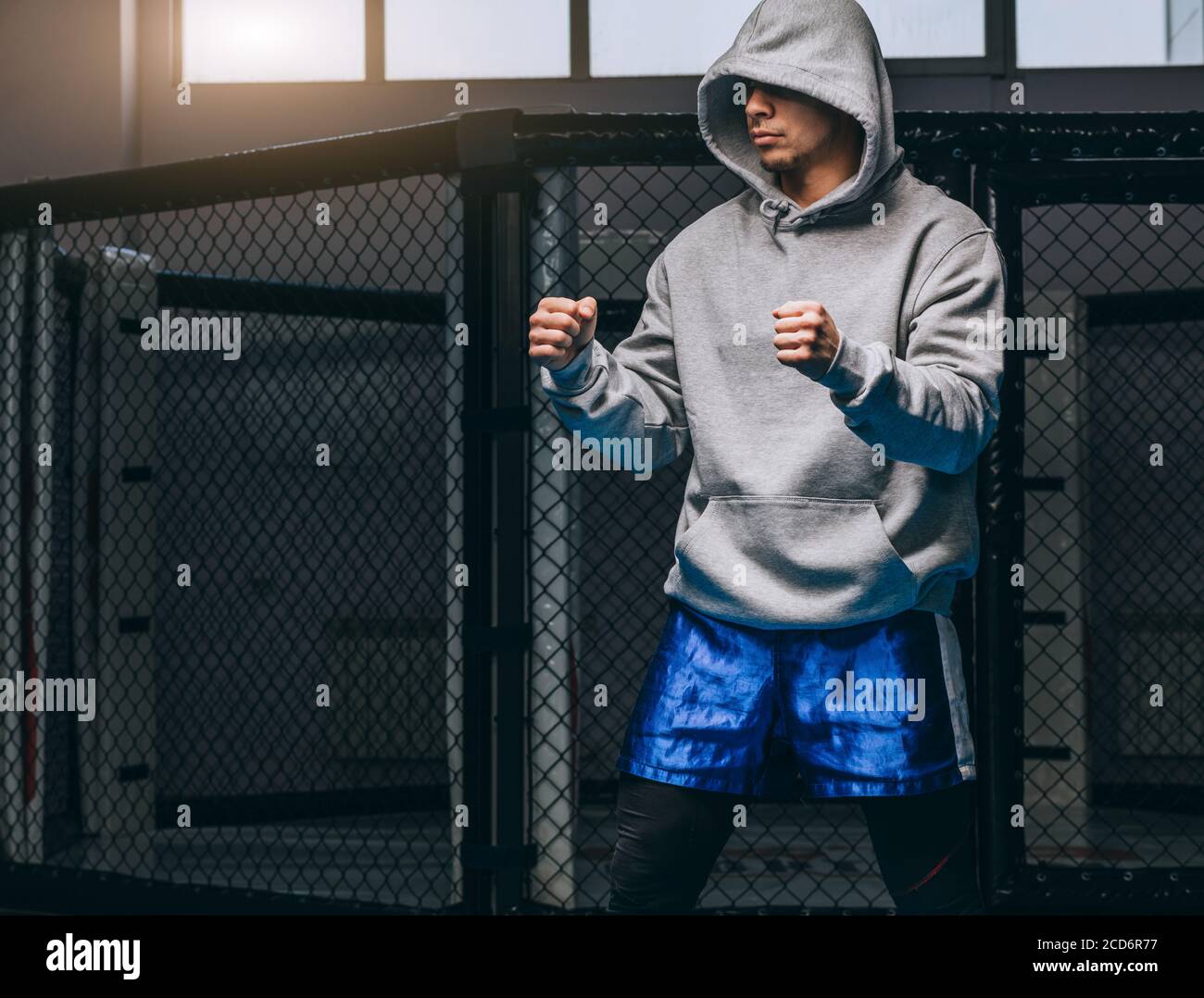 Sportsman in grey hoodie with hood hiding his eyes, doing punches near ...