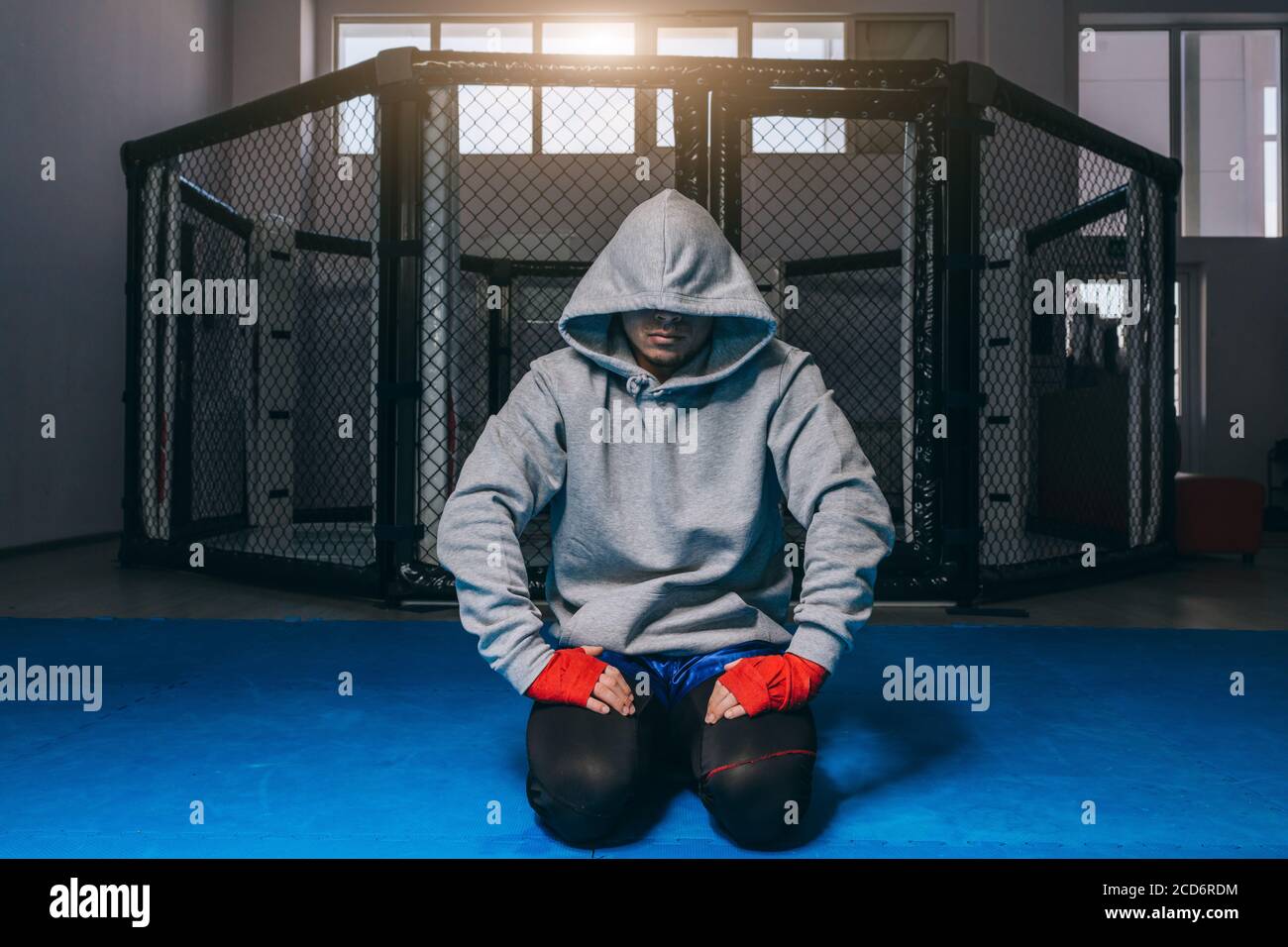 Boxer man in sportswear with hood on head posing on knees in a dark ...