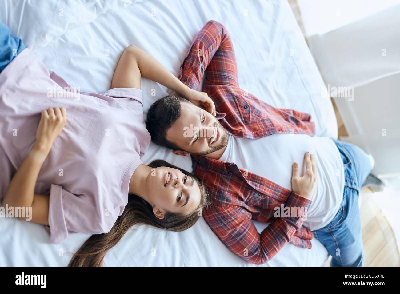 Top view of charming cheerful lovers lying on white sheet, young female ...