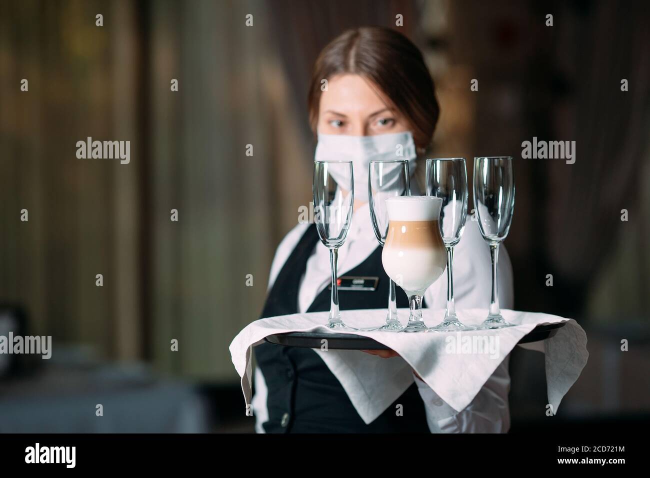 A female Waiter of European appearance in a medical mask serves Latte ...